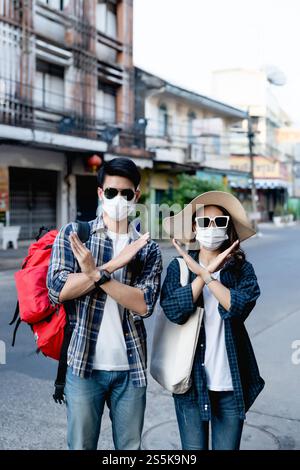 Young backpacker couple in face mask and sunglasses make a prohibition ...