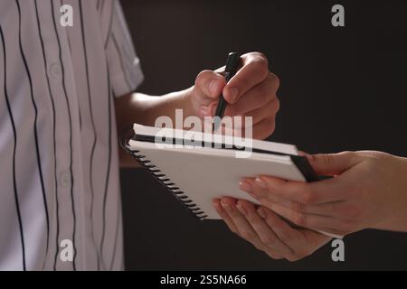 Baseball player signing autograph in notebook against black background ...