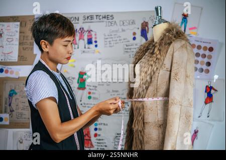 Charming female tailor using the tape measure on the mannequin to cut ...