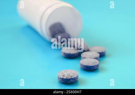 Several grey tablets fall out of the plastic jar on the blue surface ...