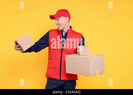 Happy postman with parcels on yellow background Stock Photo - Alamy