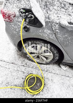 An electric vehicle connects to a charger in a bustling city during ...