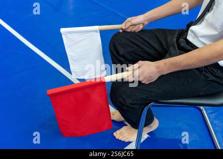 The karate referee sitting beside the mat with red and white flags in ...