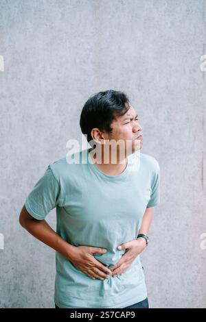 A man experiencing stomach discomfort, holding his abdomen with a ...