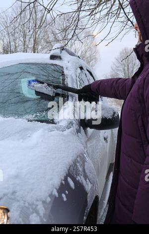 A driver removes snow from his car at night, at a Shell gas station in ...