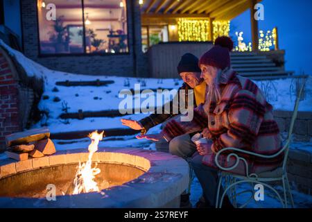 Older couple has lit a fire in garden fire pit. Seniors watching flames ...