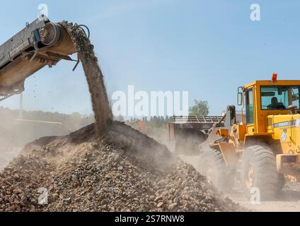 Crushed stones fall from a conveyor. In the background a Volvo wheel ...
