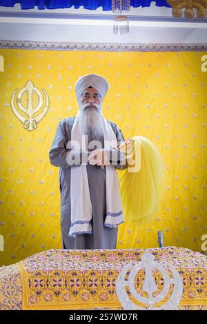 A Sikh man holds his Chaur Sahib fly whisk at an Akhand Path service ...