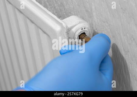 Man wearing glove bleeding an old radiator with a key. Winter energy ...