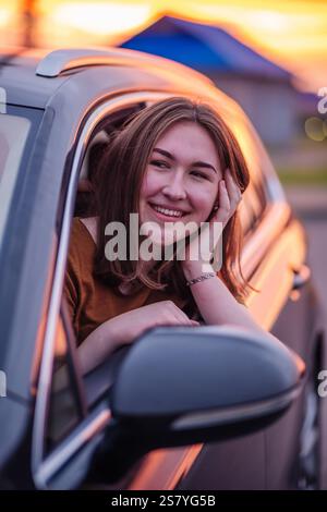 Woman smiling, relaxing inside a car holding a reusable coffee cup ...