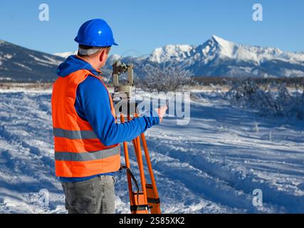 Surveyor taking measurements in snowy mountain landscape using ...