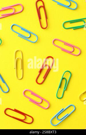 Colorful paper clips on yellow background. Office supplies and ...