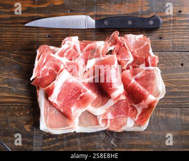 Thinly sliced cured meat arranged on rustic wooden board. Red chili ...