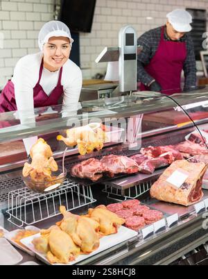 Happy female butcher holding whole chicken in meat section of ...