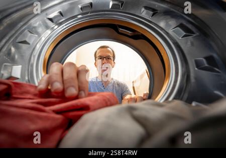 A mature man puts his clothes into a washing machine seen from inside ...