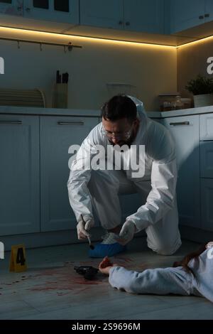Forensic expert taking fingerprints with brush from gun and dead body at crime scene indoors ...