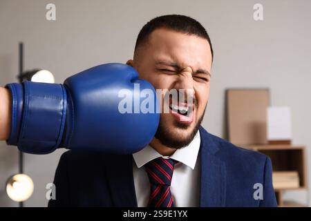 Young businessman getting hit in his face with boxing glove in office ...