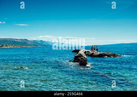 Swimmers standing on a rock at at Uvala Firule beach, Split, Croatia ...