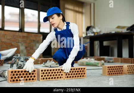 Workwoman preparing bricks for masonry at construction site indoors ...