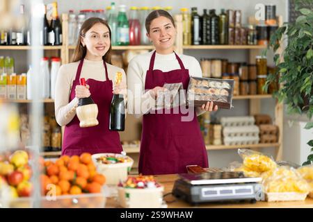 Two sales girls pose behind a store counter with groceries, sweets and ...