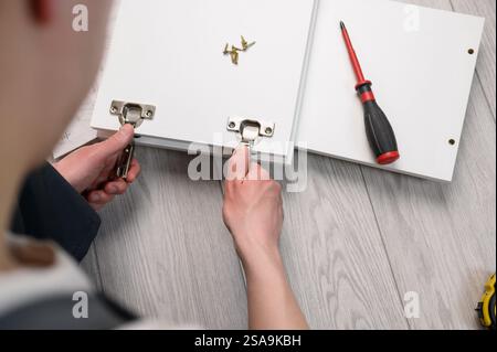 Assembling furniture. A worker inserts a hinge into a wooden closet ...