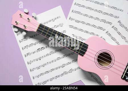 Ukulele and music sheets on pink background, top view. Space for text ...