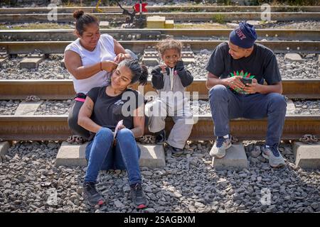 A migrant woman braids another woman's hair as they sit and wait along ...