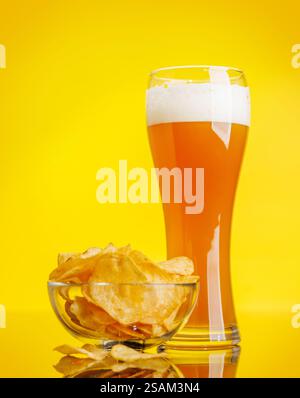 A glass of cold beer alongside a pile of crispy potato chips on a ...