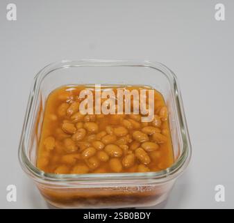 Glass container filled with baked beans in a rich sauce against a white ...