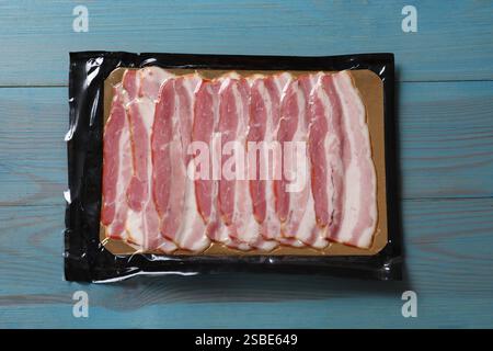 Pack of sliced bacon on light blue wooden table, top view. Space for ...