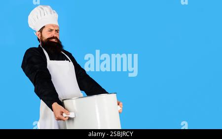 Bearded chef in uniform with big saucepan or pot. Cooking utensils ...