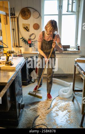 Carpenter woman cleanup workshop after woodwork. Handywoman sweep ...