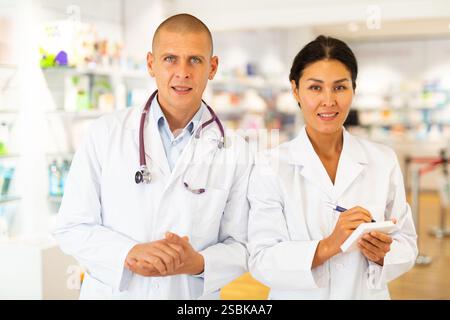 Portrait of two pharmacists - men and women in white coats in pharmacy ...
