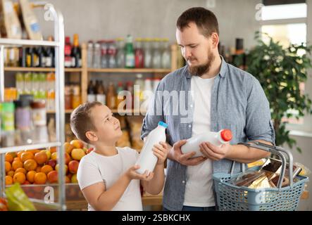Man with son hold packages bottles and choose consider milk in store ...