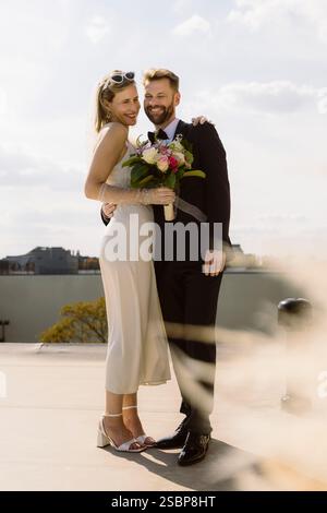 Happy newly married couple standing with wedding guests on rooftop ...