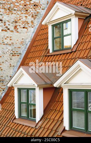 A red tiled roof with three windows set against a clear sky, showcasing ...