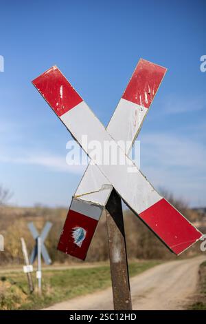 A partly bended railway crossing sign in red and white marks a dirt ...