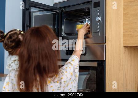 Child using a microwave oven in the kitchen at home. Kid aged two (two ...
