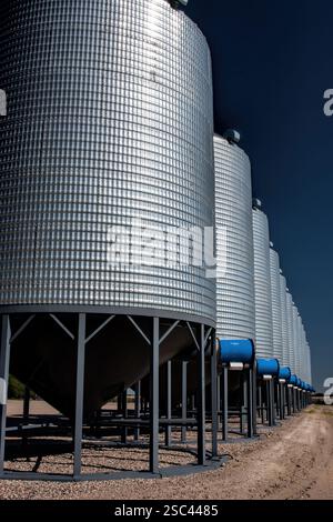 A row of large metal tanks are lined up in a field. The tanks are empty ...