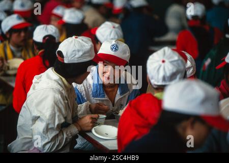 Group of shoe factory workers wearing uniforms and caps eating at a ...