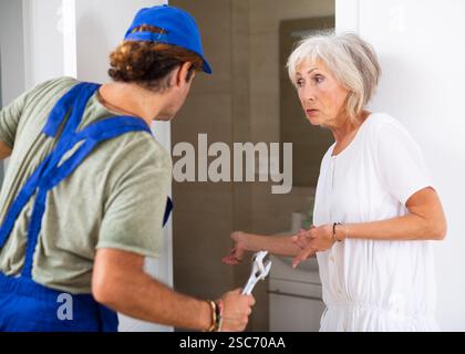 Elderly woman talking with plumber at home Stock Photo - Alamy