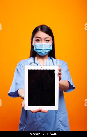 asian female doctor presenting tablet computer screen while seated at ...
