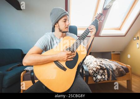 Musician sits by a sunlit window, deeply focused on playing an acoustic ...