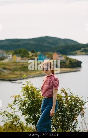Young redhead woman wearing sunglasses pointing and showing with thumb ...