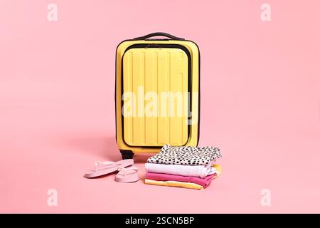Suitcase, flip-flops and folded clothes on pink background Stock Photo ...