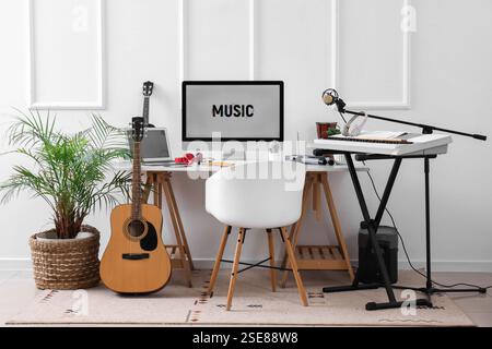 Workplace with computer and musical instruments near light wall in ...