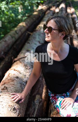 Portrait of an active 36 yo woman, sitting on tree trunks in the woods ...
