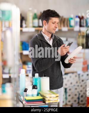 Checking expiration date of shampoo or shower gel - male shopper scans QR code on label of ...