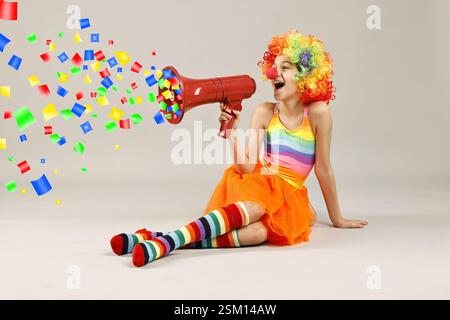 Cute girl dressed like clown shouting in megaphone with confetti flying ...