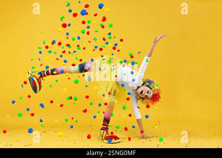 Happy girl dressed like clown under falling confetti on orange ...